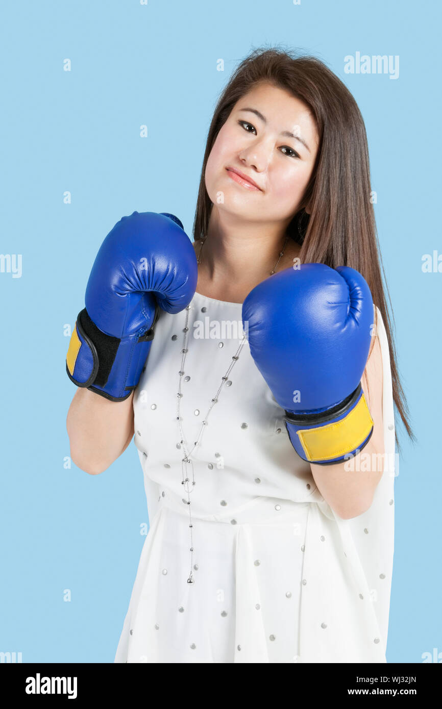 Portrait of a beautiful young woman wearing boxing gloves over blue ...