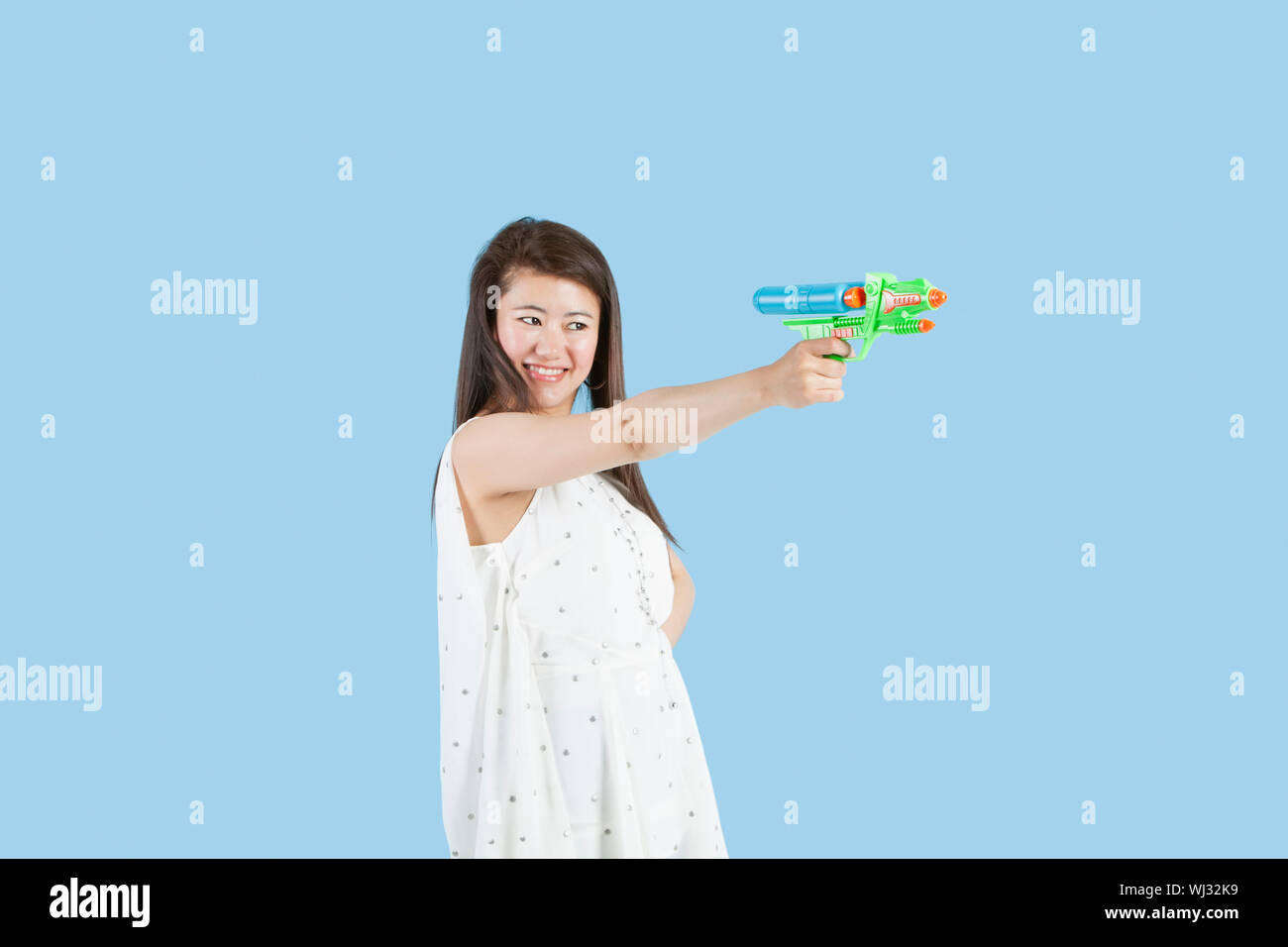 Happy young woman aiming with a toy gun over blue background Stock ...