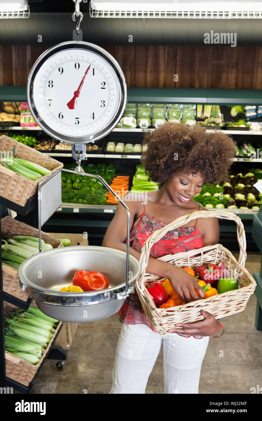 African American woman weighing bell peppers on scale at supermarket ...
