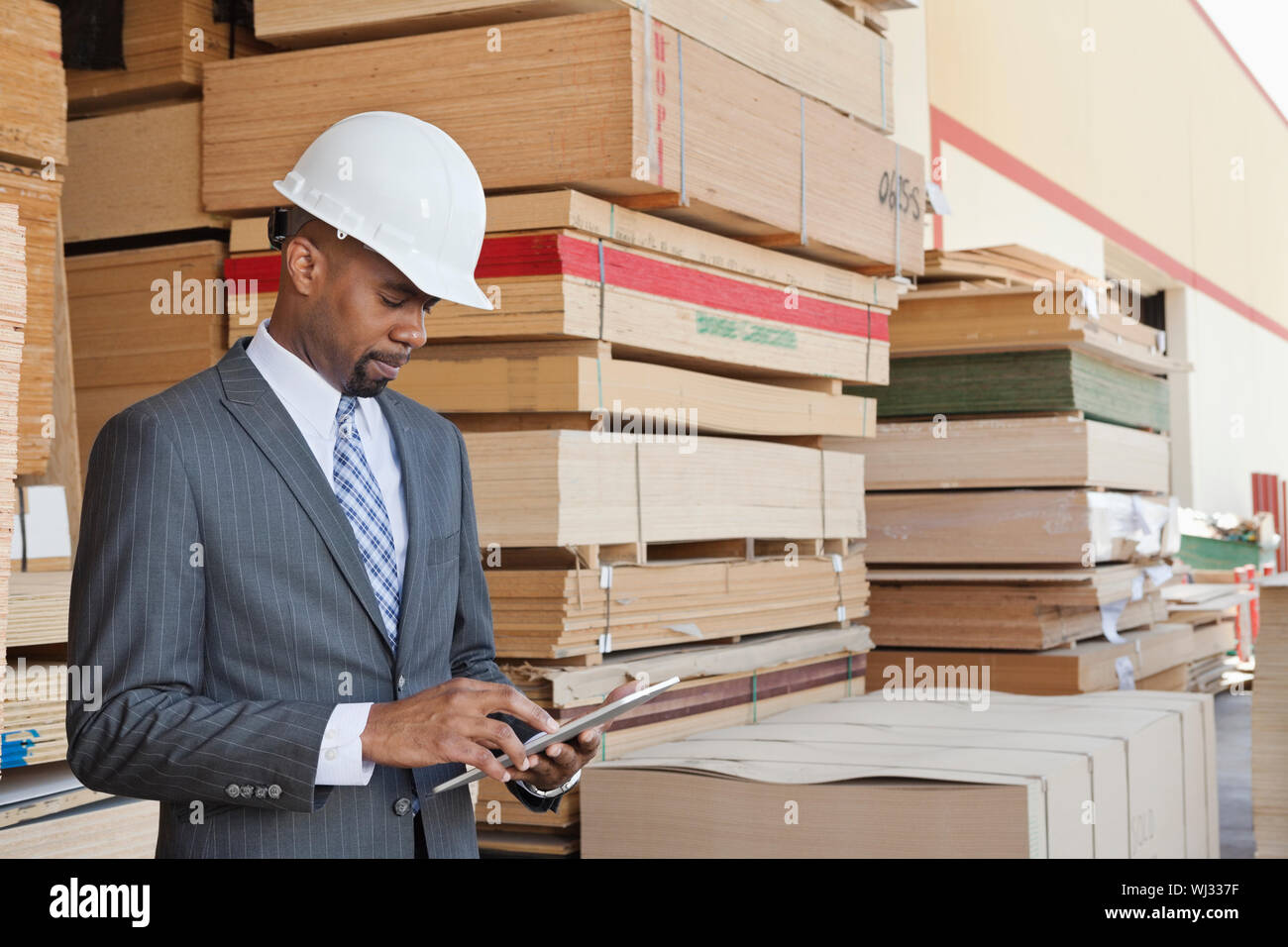 African American male contractor using tablet PC with stacked wooden ...