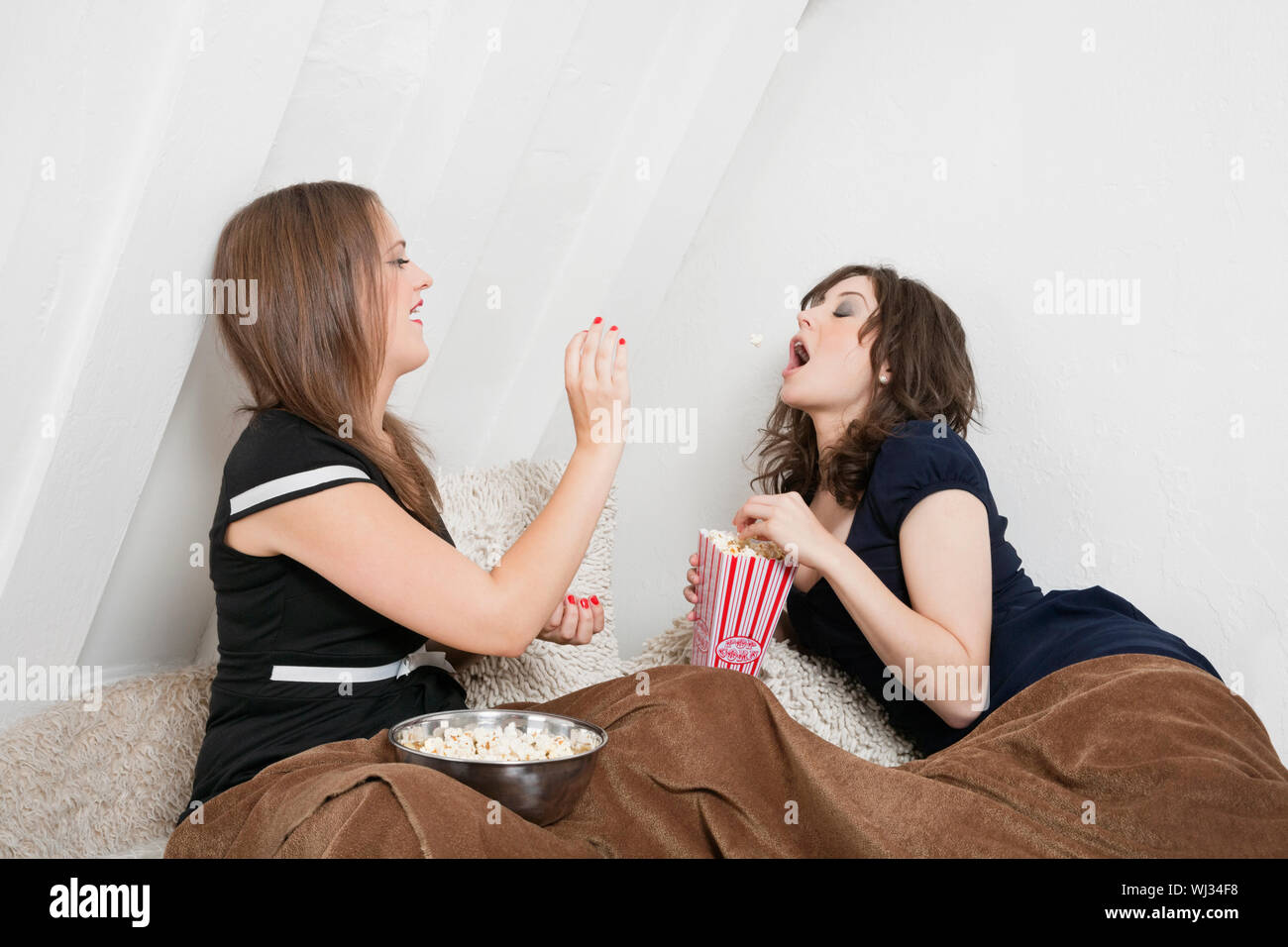 Playful Young Female Throwing Popcorn Into Friends Mouth In Bed Stock