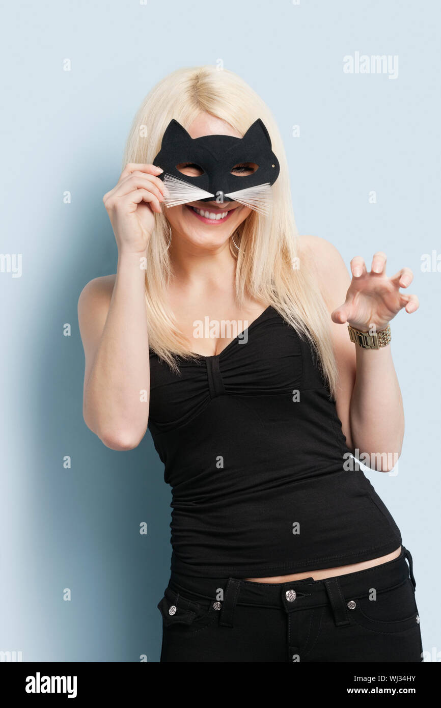 Portrait of young woman wearing a cat mask over light blue background ...