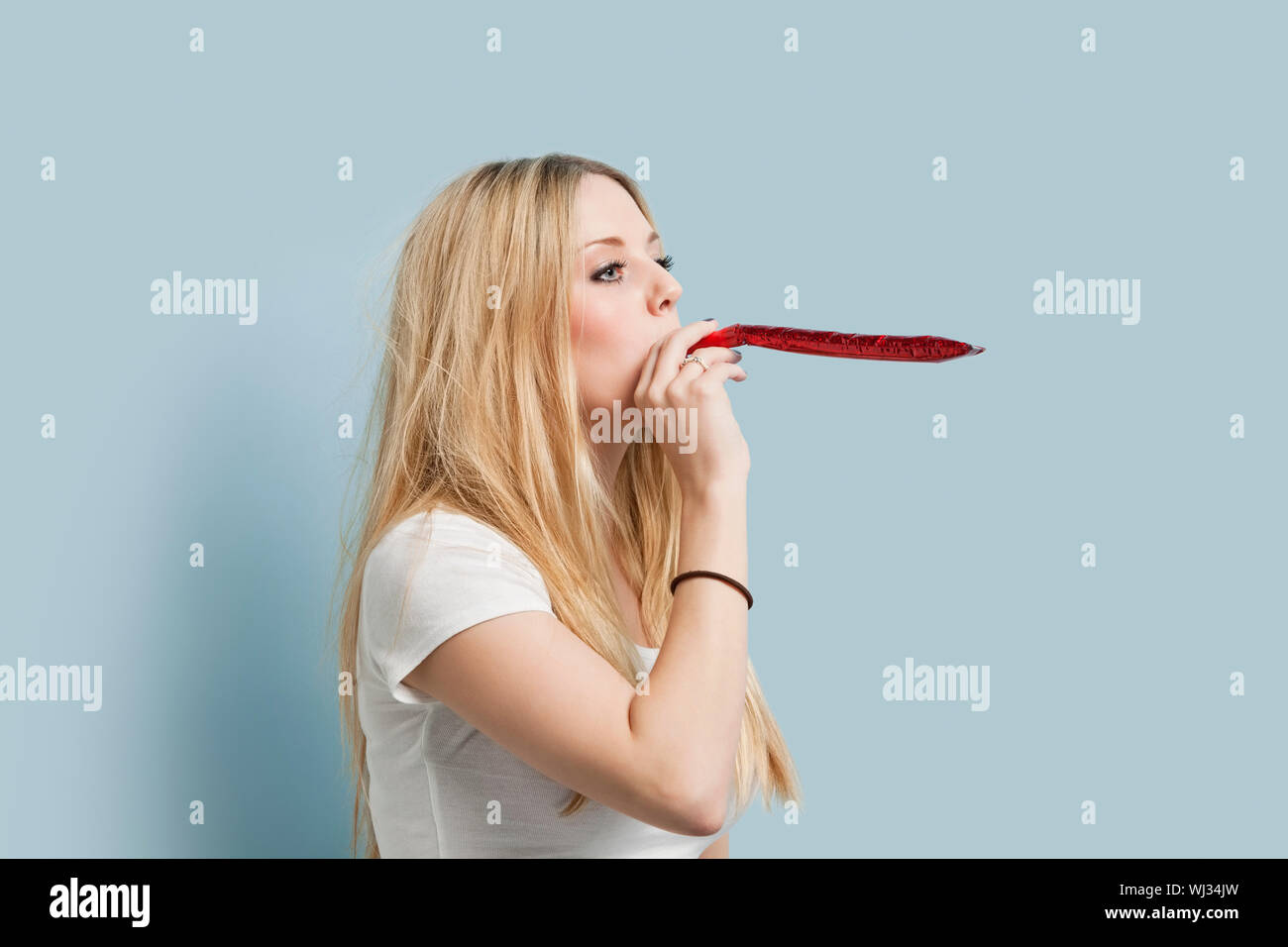 Young woman blowing party blower against light blue background Stock ...