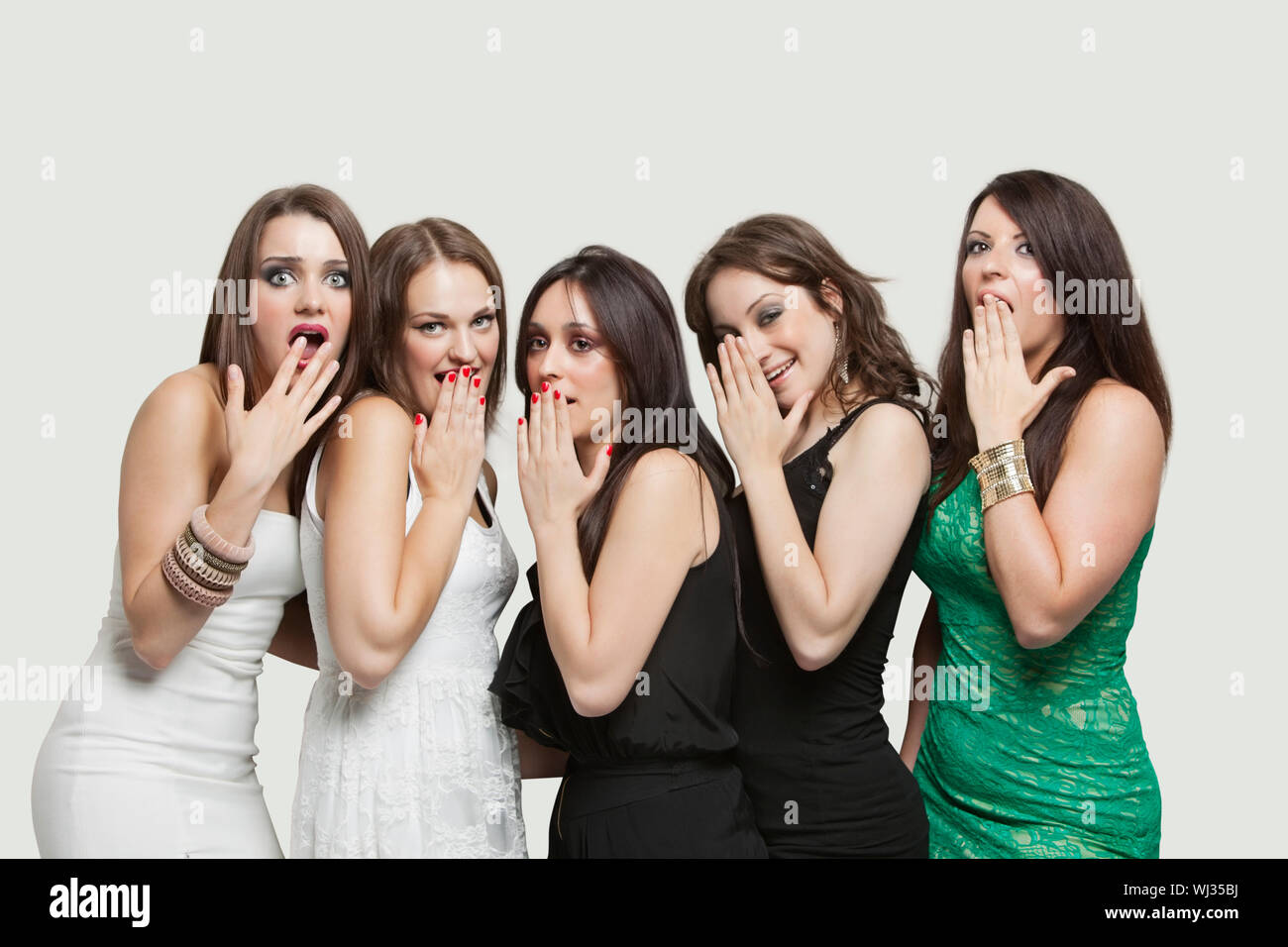 Portrait of five shocked young women with hands over mouth against gray ...