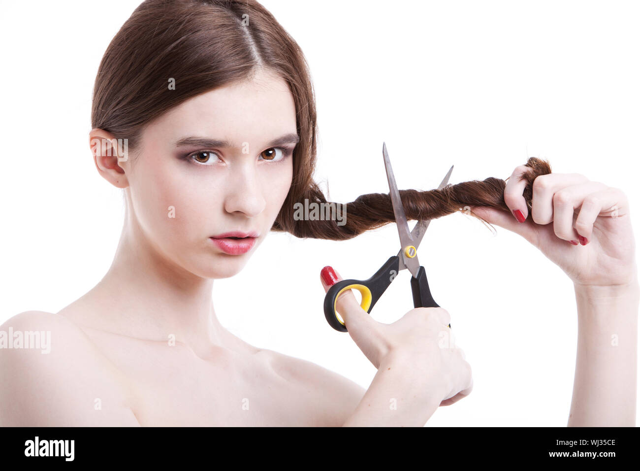 Portrait of beautiful young woman with scissors cutting her hair over ...