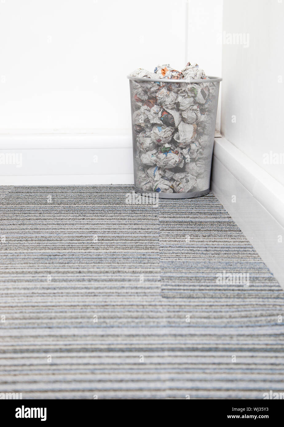 Wastebasket full of crumpled paper in corner on carpet floor in room ...