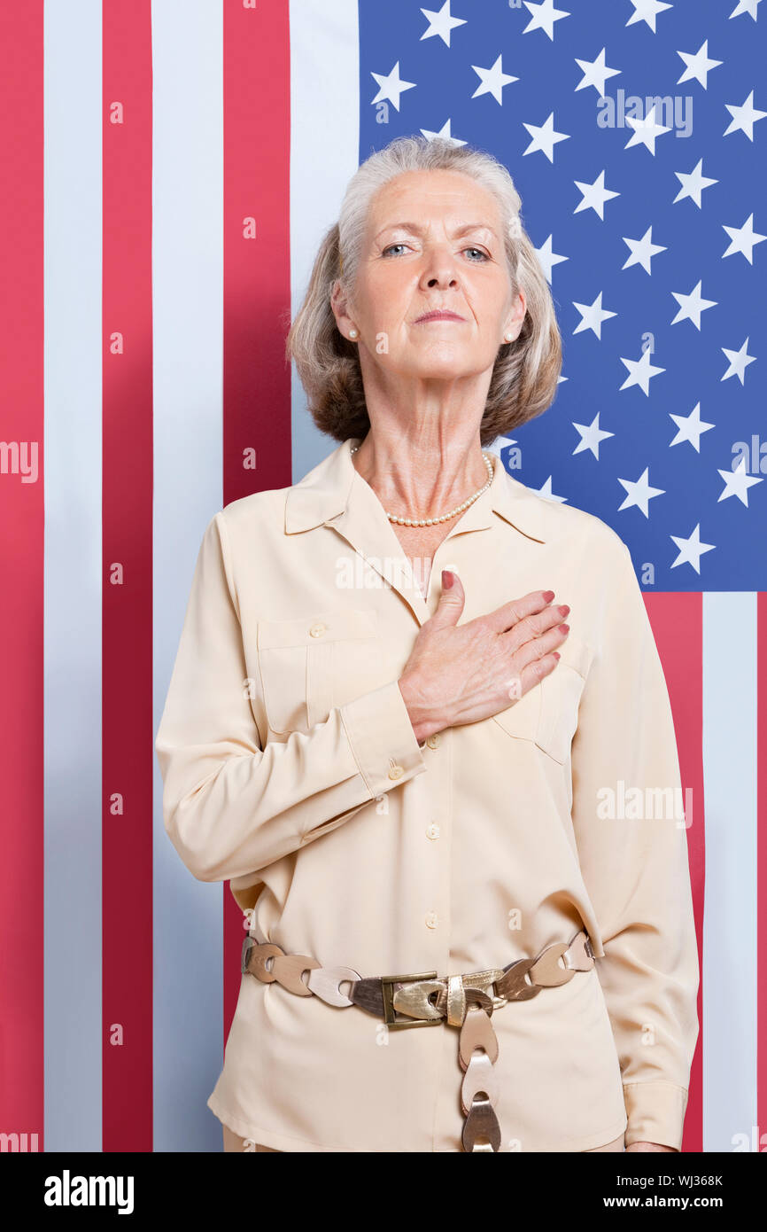 Portrait of senior woman with hand over heart against American flag ...