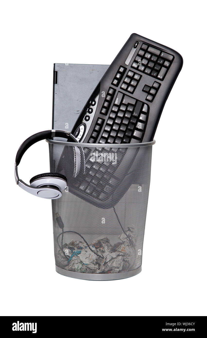 Computer keyboard and headphones in wastebasket against white ...