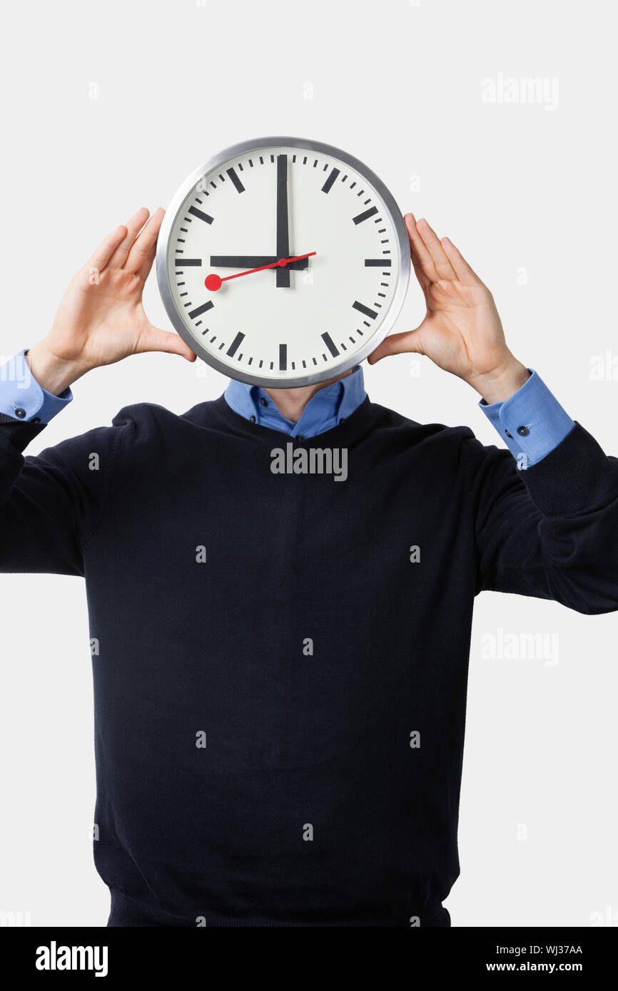 Young man covering his face with clock standing against white ...