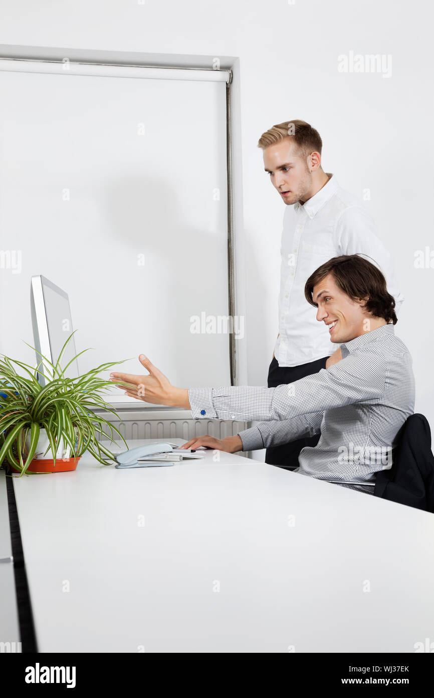 Happy businessman showing computer screen to coworker at desk Stock ...