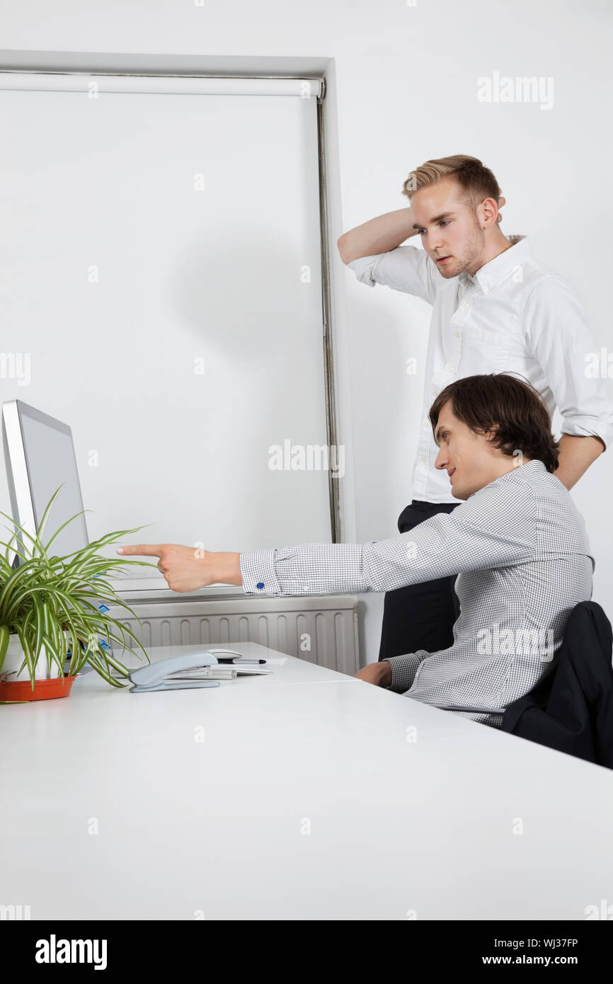 Young businessman showing computer screen to confused coworker at desk ...