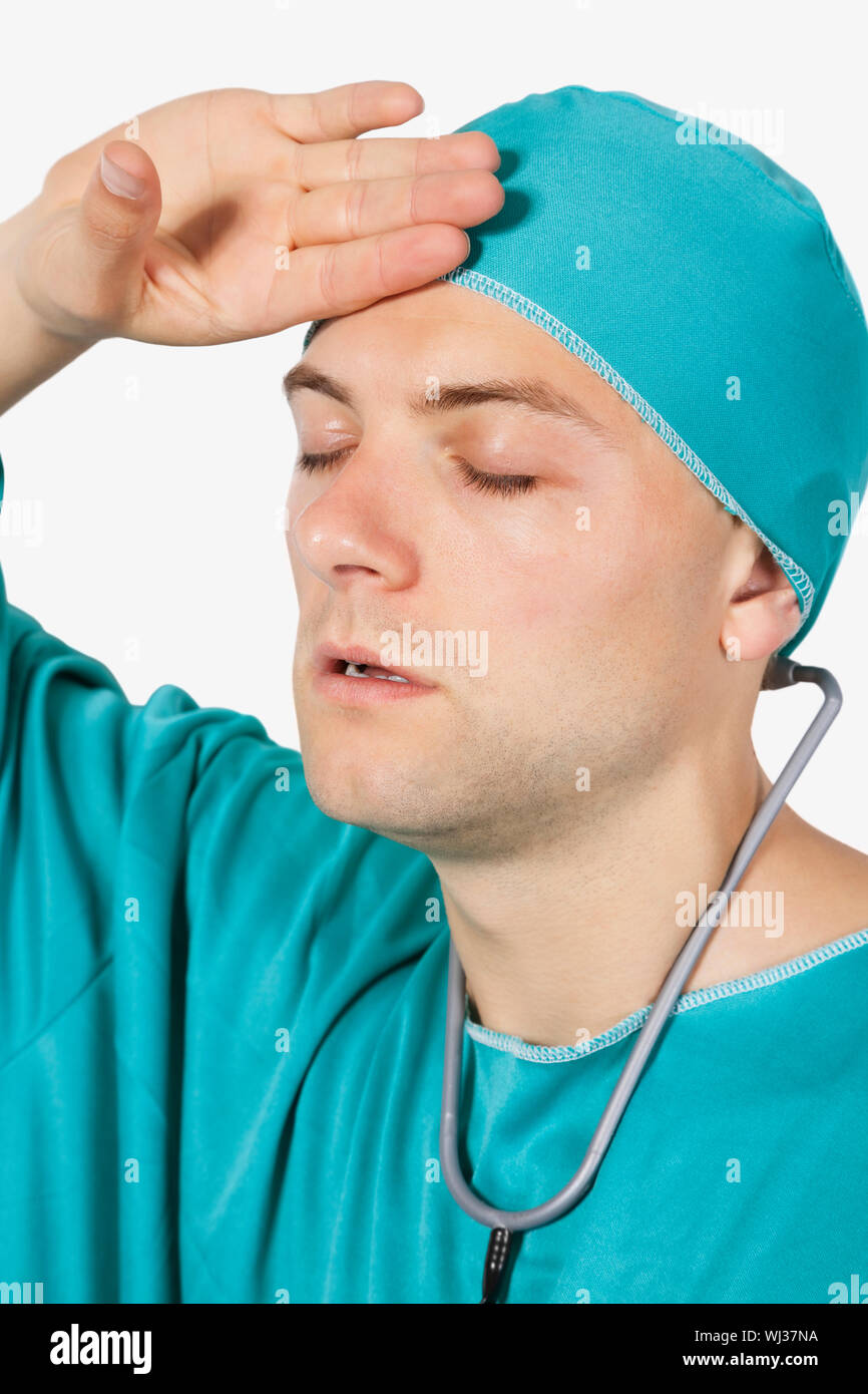 Young tired surgeon wearing scrubs against white background Stock Photo ...
