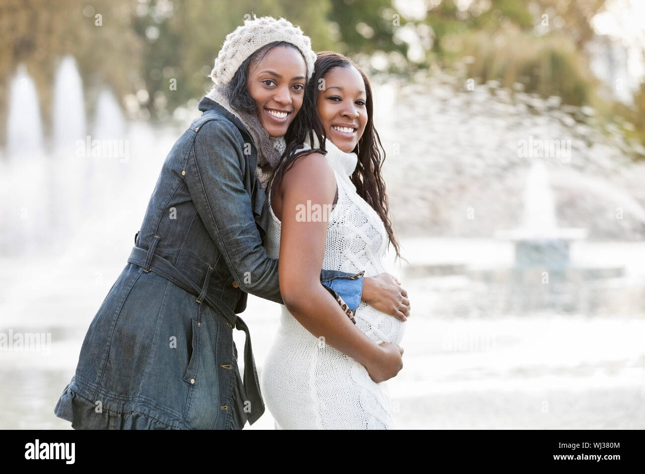 Portrait of happy young woman embracing pregnant woman from behind ...