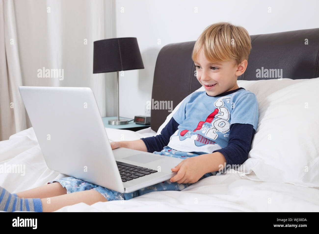 Smiling Caucasian boy using laptop computer in bed Stock Photo - Alamy