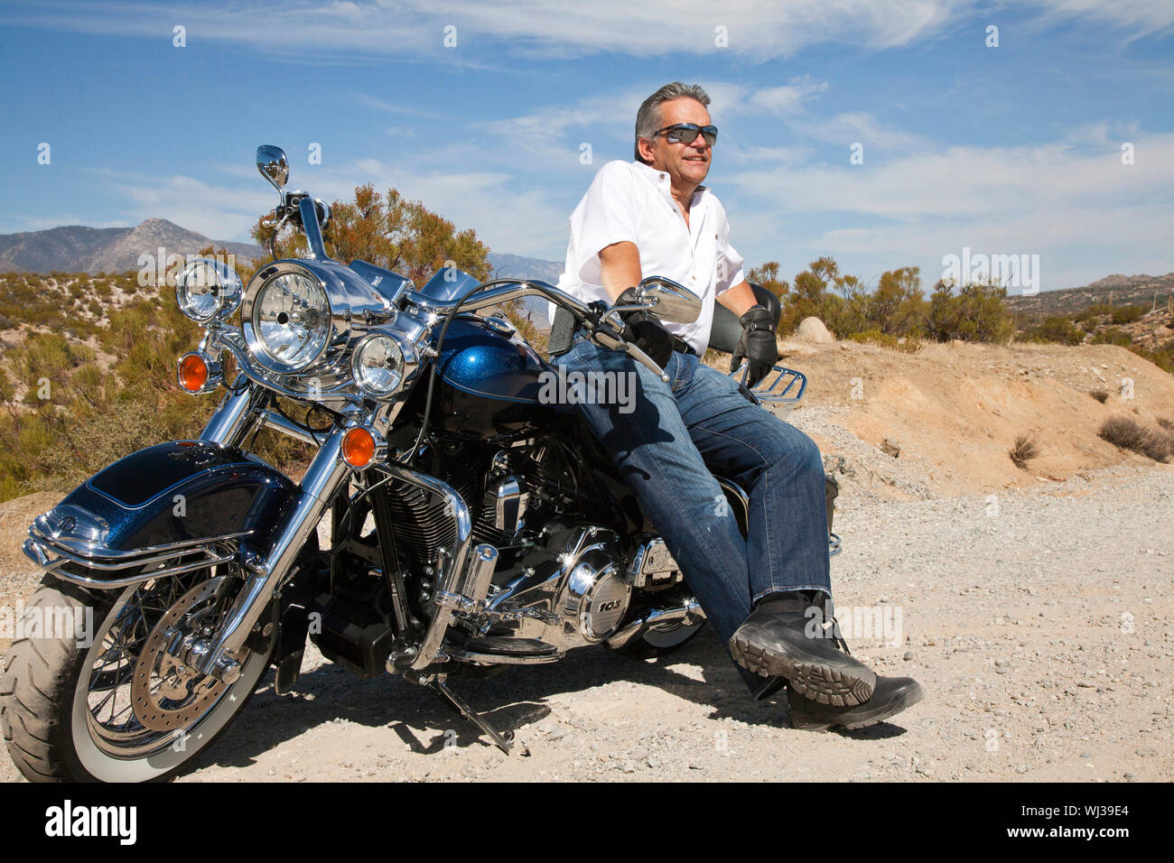 Senior man leaning on motorcycle on desert road Stock Photo - Alamy