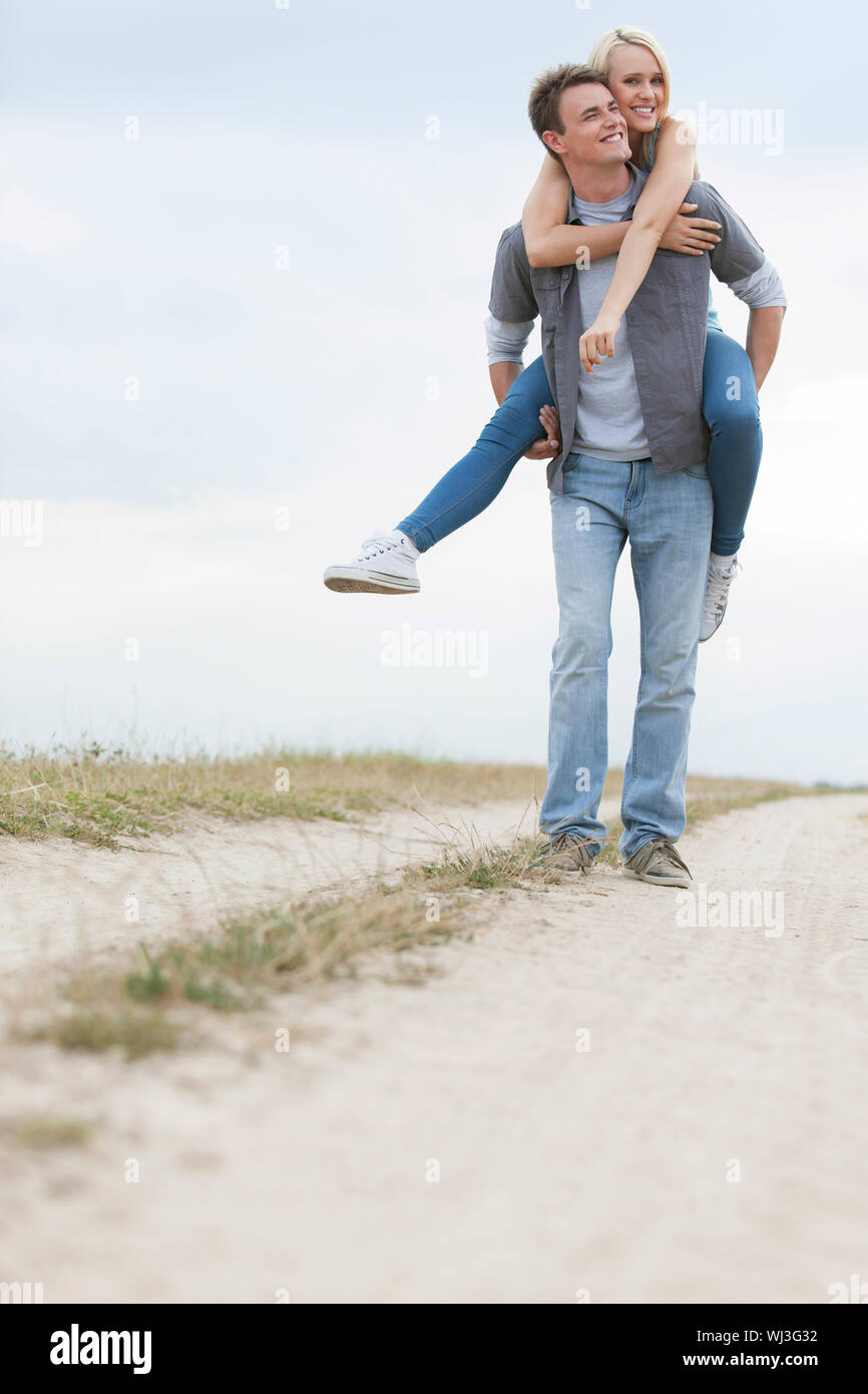 Young man piggybacking woman on trail at field Stock Photo - Alamy
