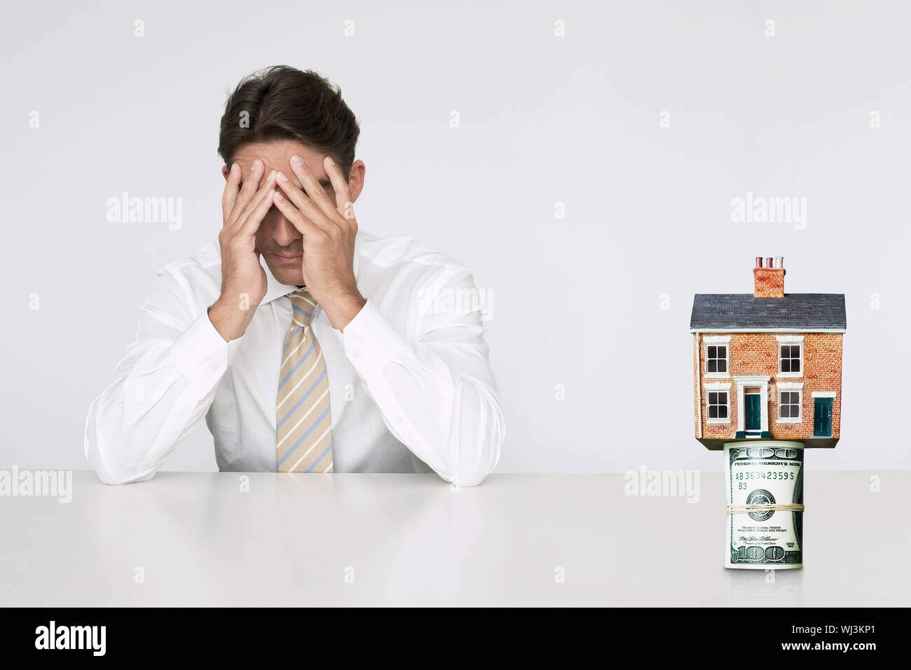 Worried businessman at table with house on top of bills representing ...