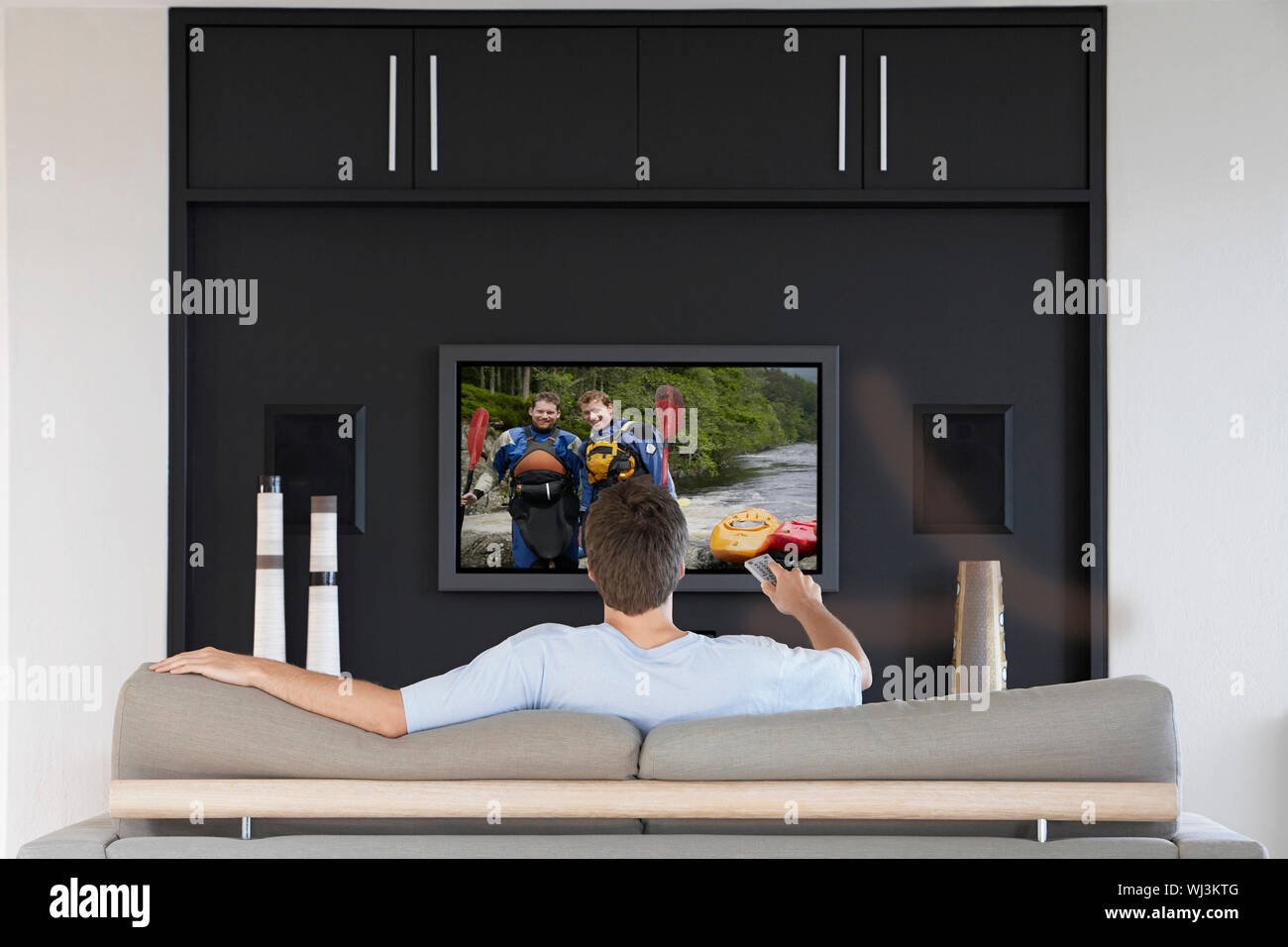 Back view of mid-adult man changing channels with television remote ...