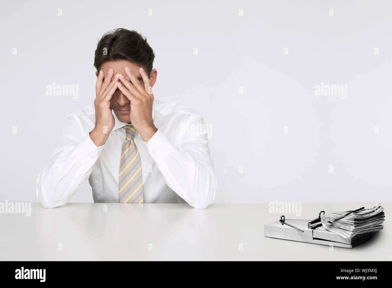 Worried businessman at table with wad of cash in mouse trap ...