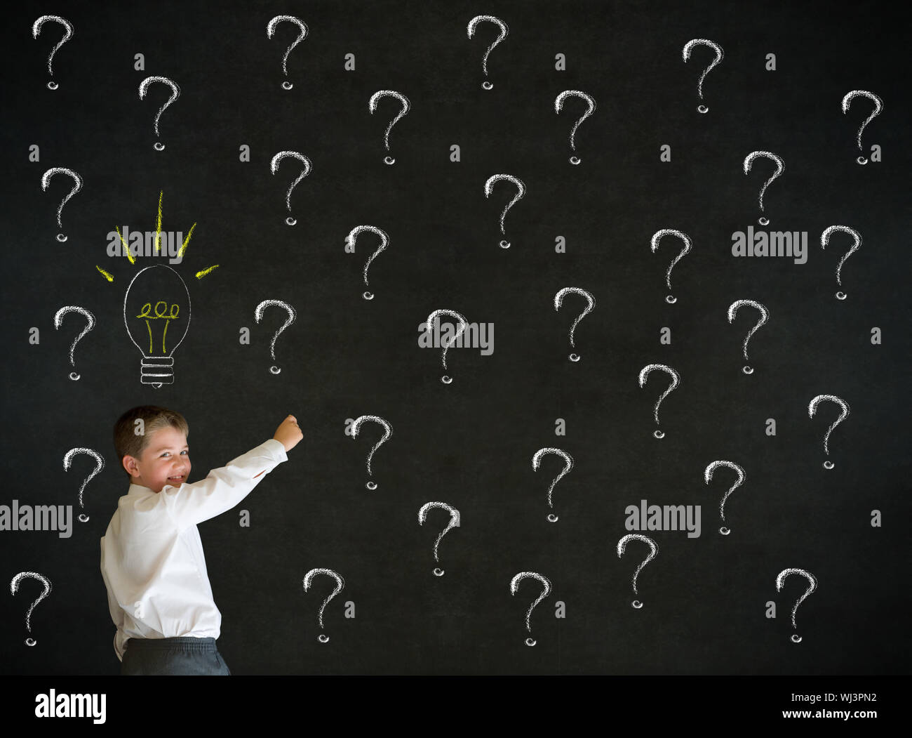 Writing boy dressed up as business man questioning ideas on blackboard ...