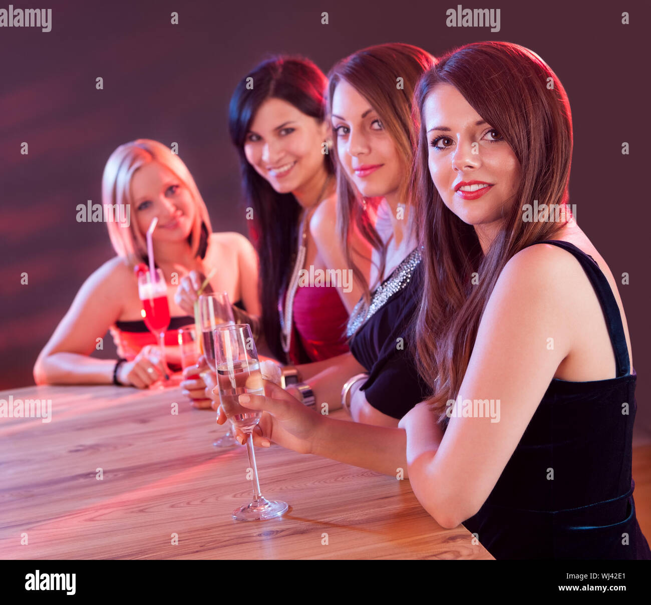 Four attractive young lounge ladies seated at a bar counter in a ...