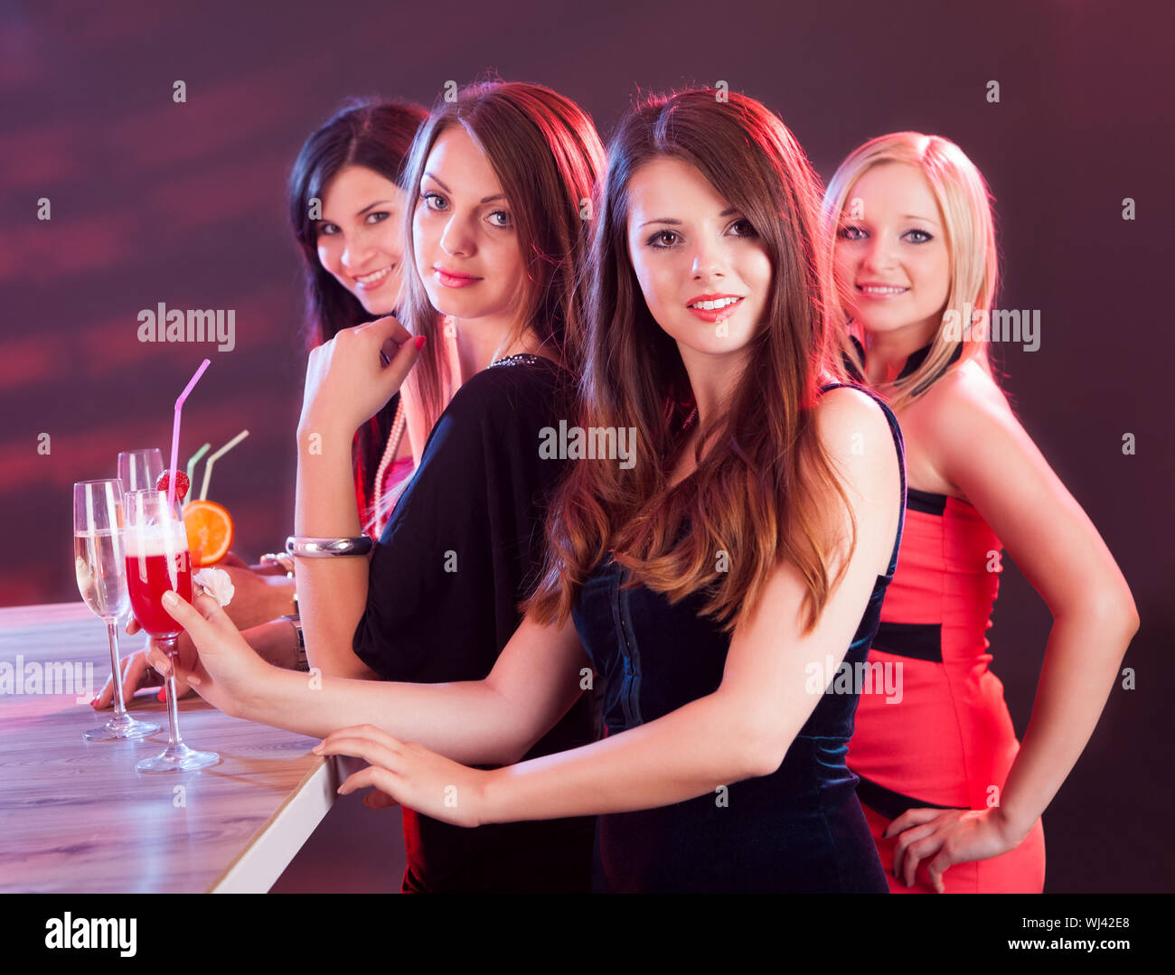 Four beautiful fashionable women on a night out standing at a bar ...