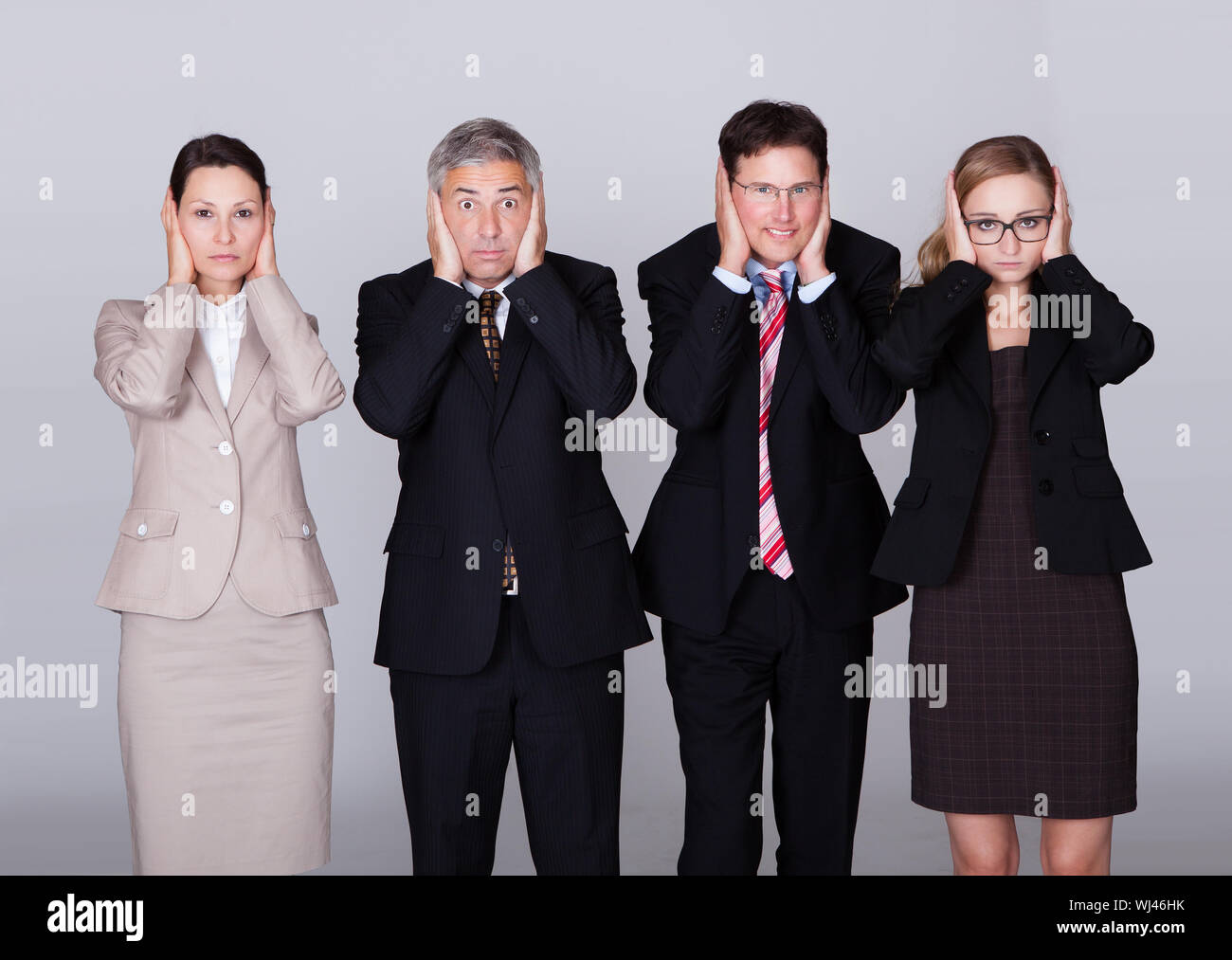 Four diverse businesspeople standing in a row holding their ears in a ...