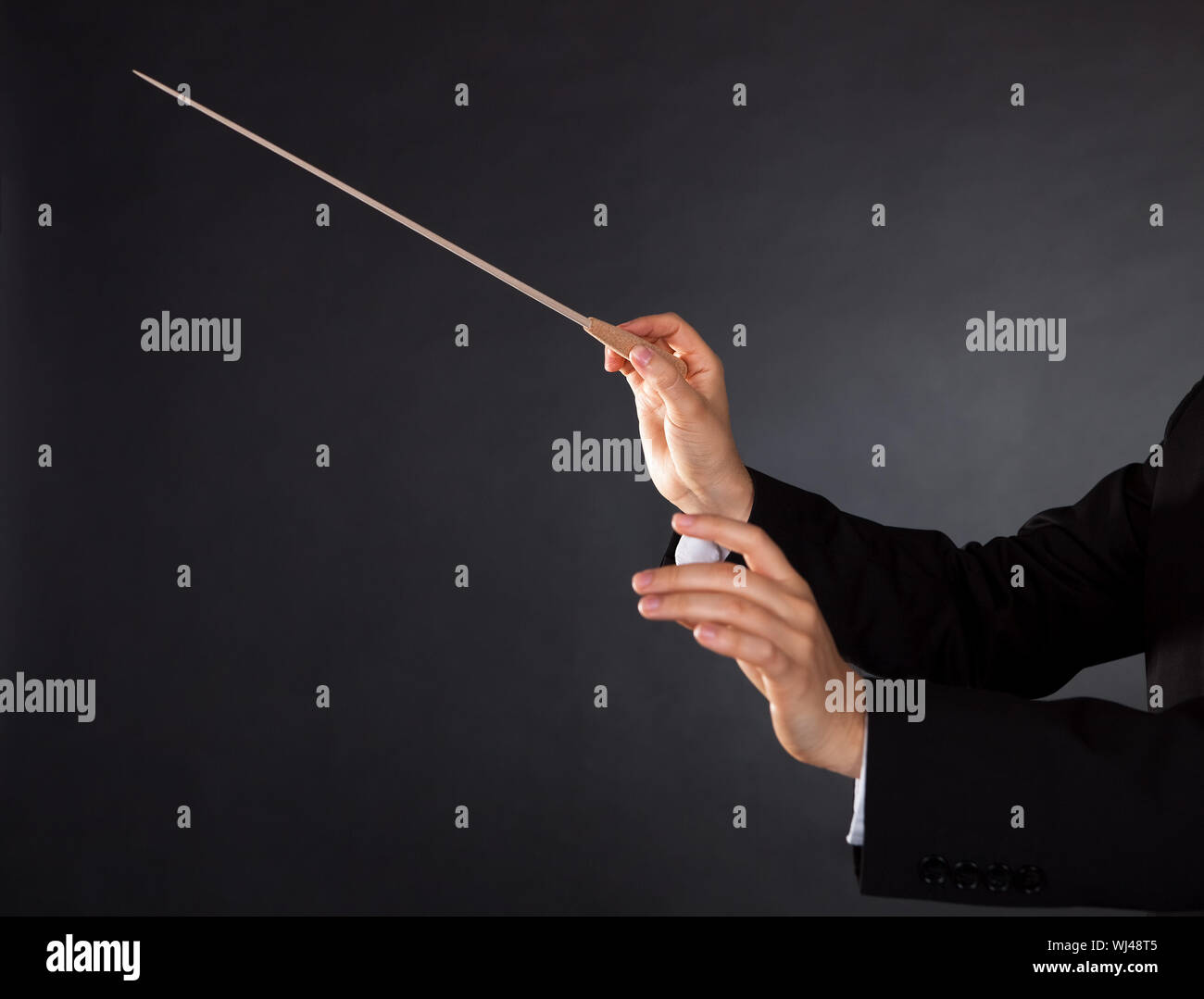 Closeup of the hands of a music conductor with a baton against a dark ...