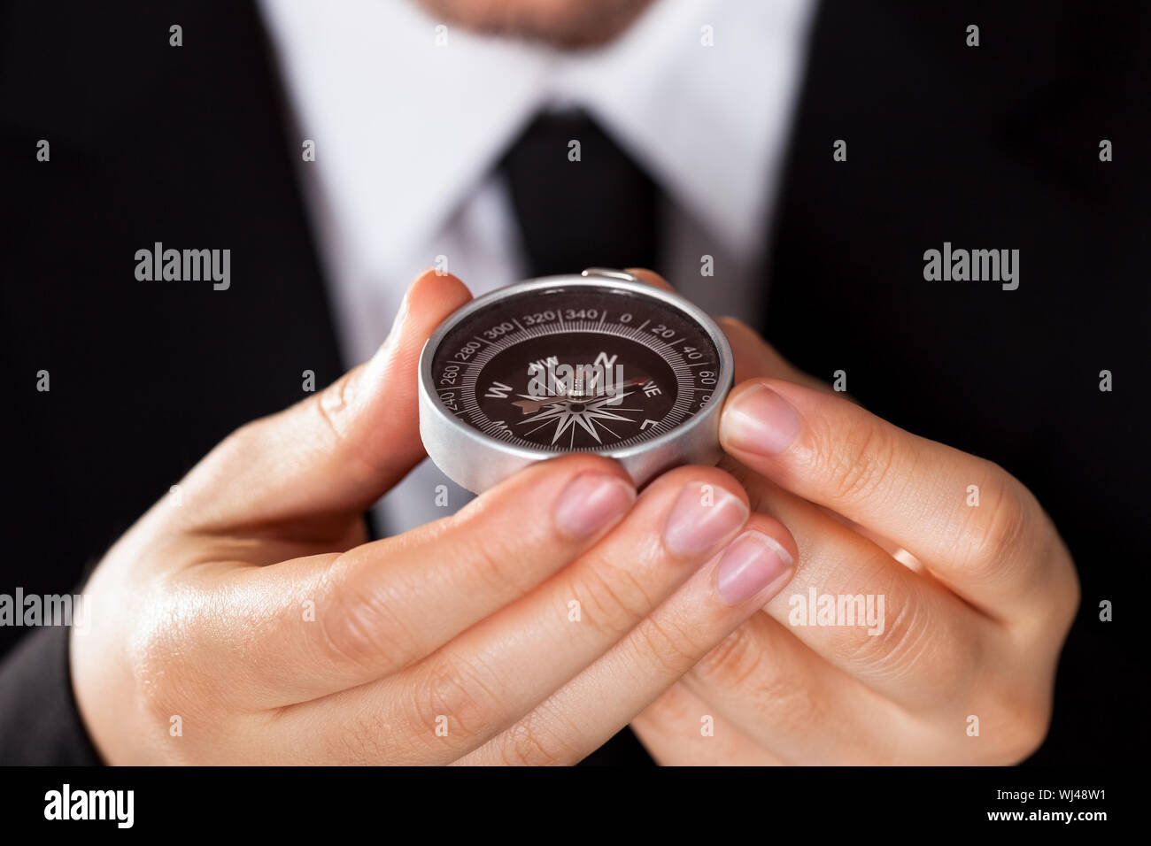 Businessman looking at a compass which he is holding in his hand with ...