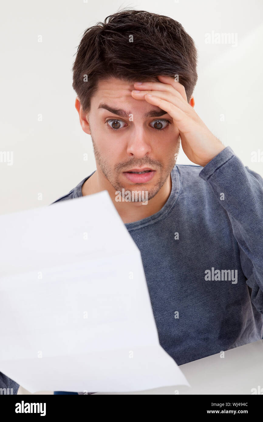Horrified young man reading a document with an aghast expression and ...