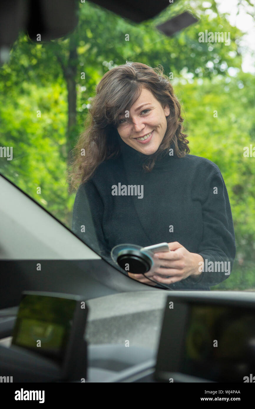 Portrait smiling young woman with smart phone accessing car share Stock ...