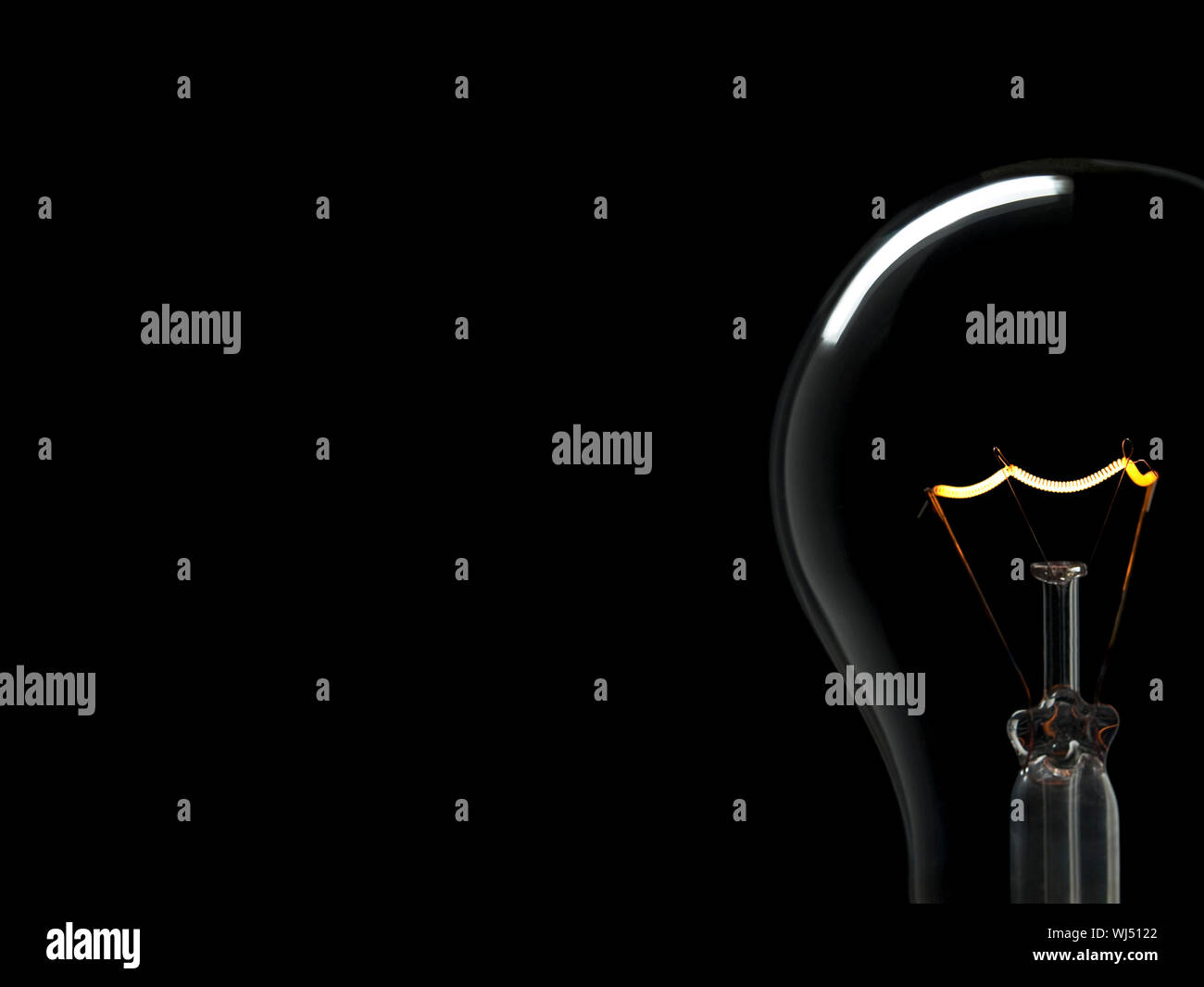 A light bulb over a black background. Tungsten glowing filament. Copy ...