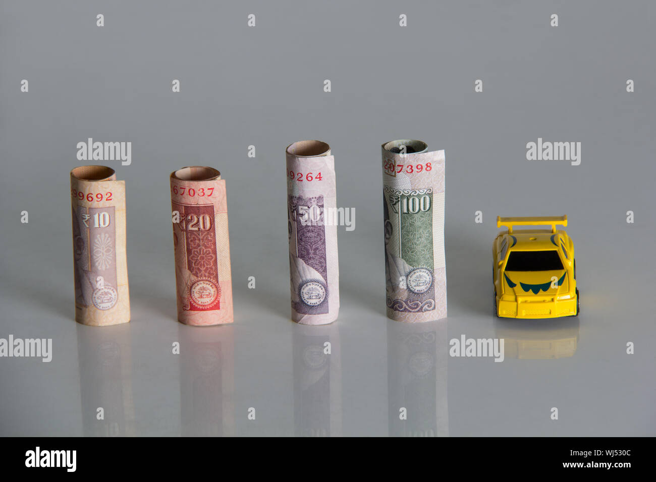 Rolls of banknotes arranged in progressing bar graph shape with toy car ...