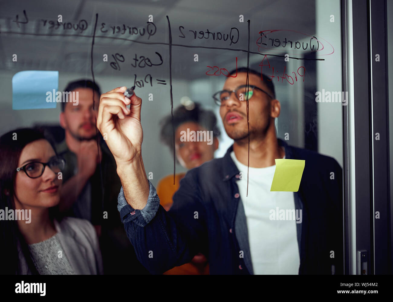 Business man writing on transparent glass wall with coworkers standing ...
