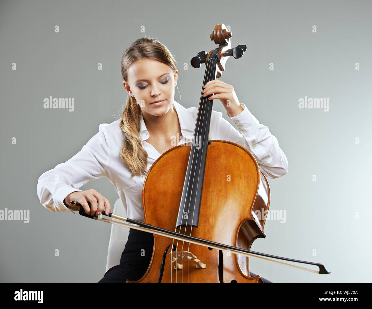 Beautiful young woman cellist on grey background Stock Photo - Alamy