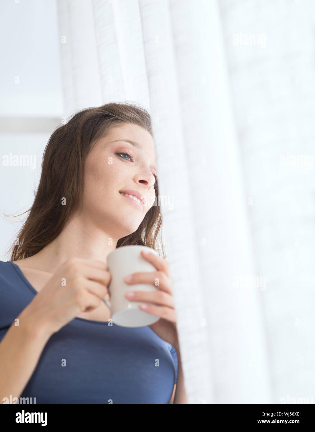 Beautiful woman with cup of coffee looking out of window Stock Photo ...