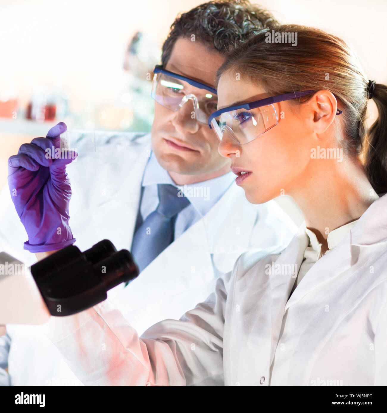 Attractive young scientist and her suprvisor looking at the microscope ...