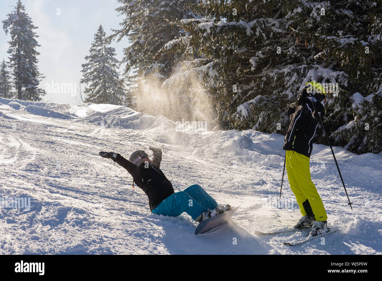 Teenagers sit with snowboard in the snow and throws happy powder snow ...