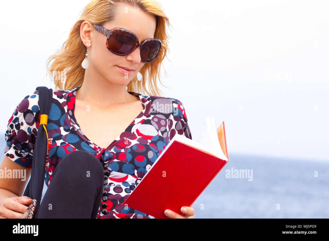 Attractive young lady reading a book by the sea Stock Photo - Alamy