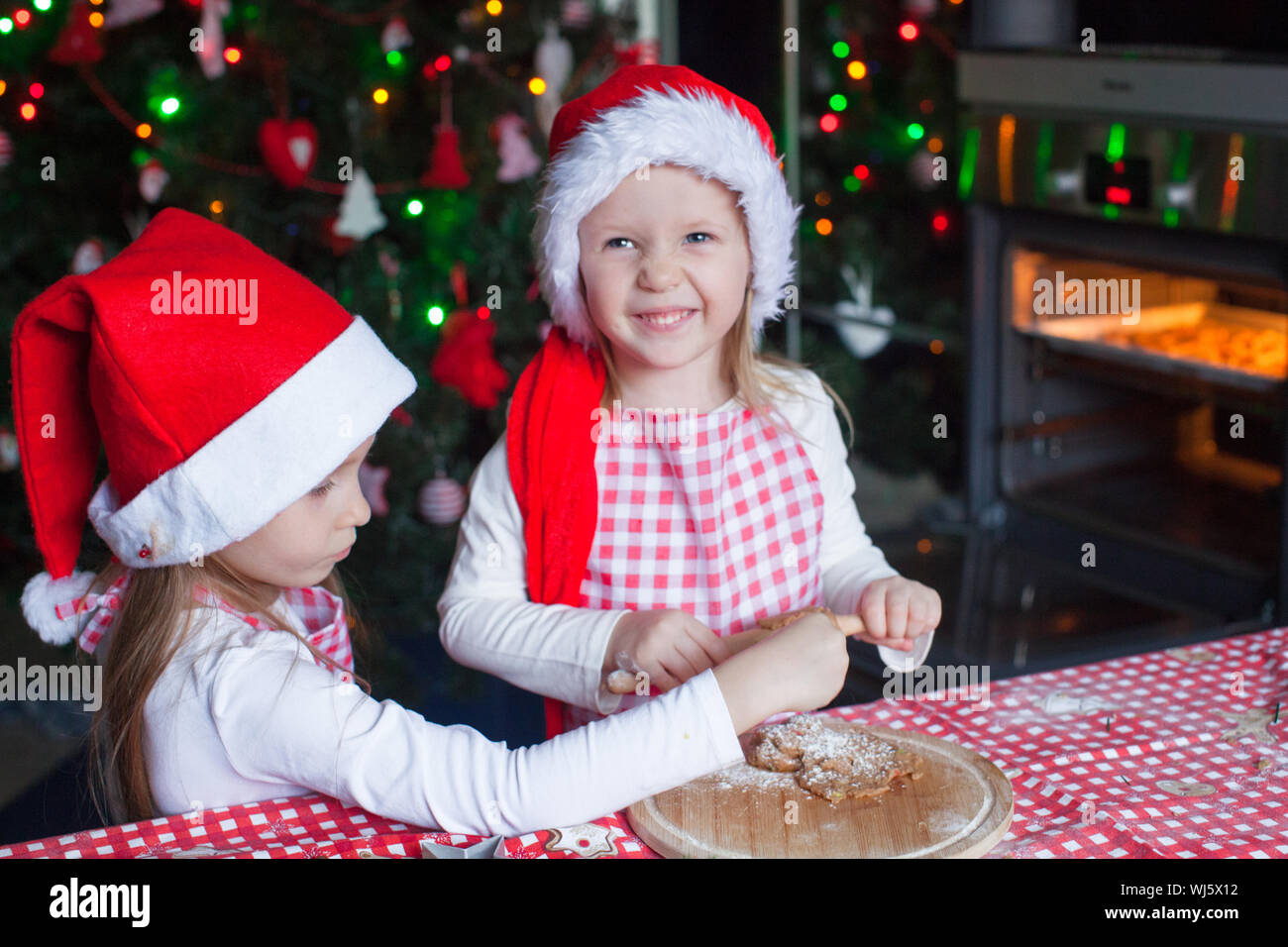 Little girls baking gingerbread cookies for Christmas in Santa hat ...