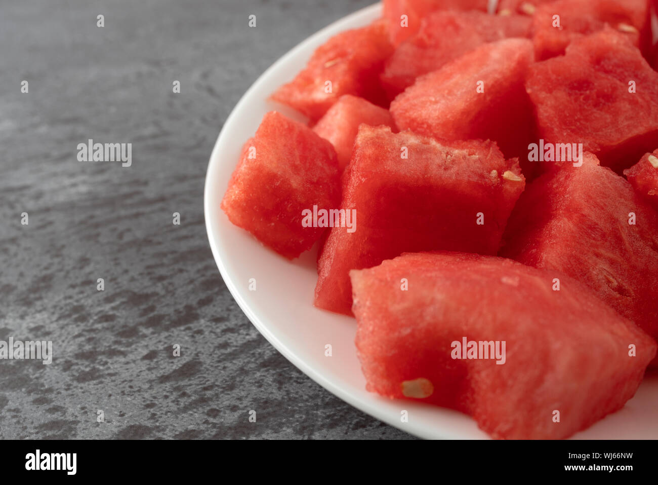 Side view of a plate of watermelon chunks on a gray mottled table ...