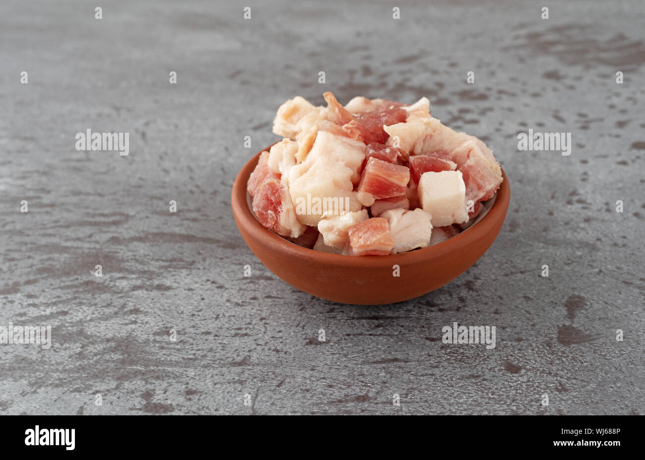 Side view of pancetta sliced into cubes in a small bowl on a gray table ...