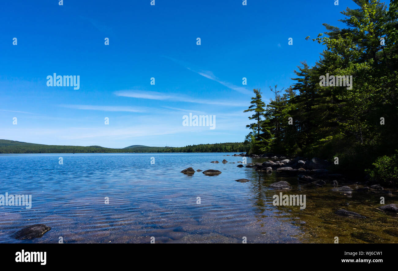 Wide view of the shoreline of Branch Lake with blue sky above and wispy ...