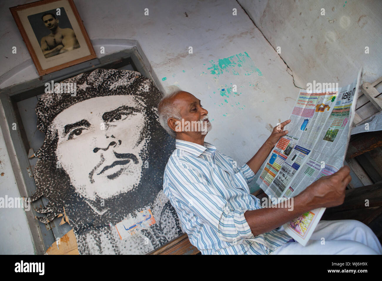India, Kerala, Fort Cochin, Man reading a newspaperwith an image of Che ...