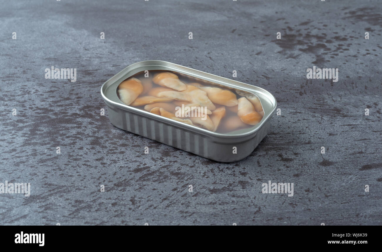 Side view of an open tin of razor clams in water on a gray table ...