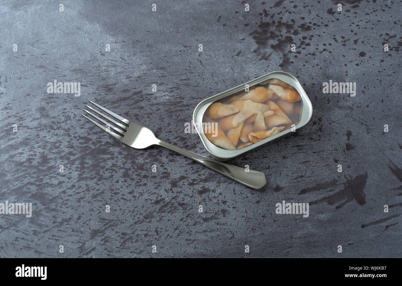 Side view of an open tin of razor clams in water on a gray table ...
