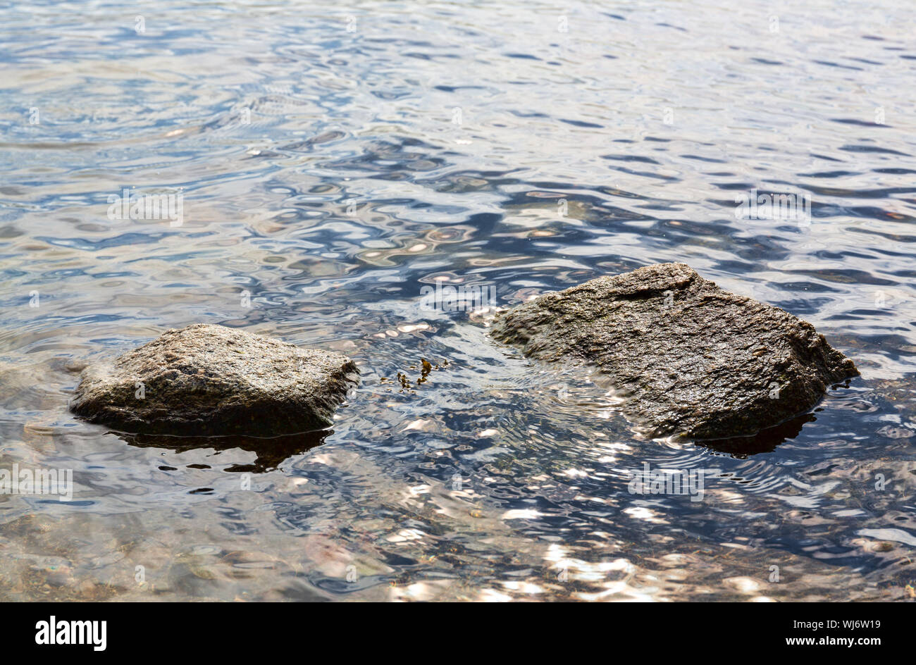 View of two large rocks surrounded by rippling water with bright ...