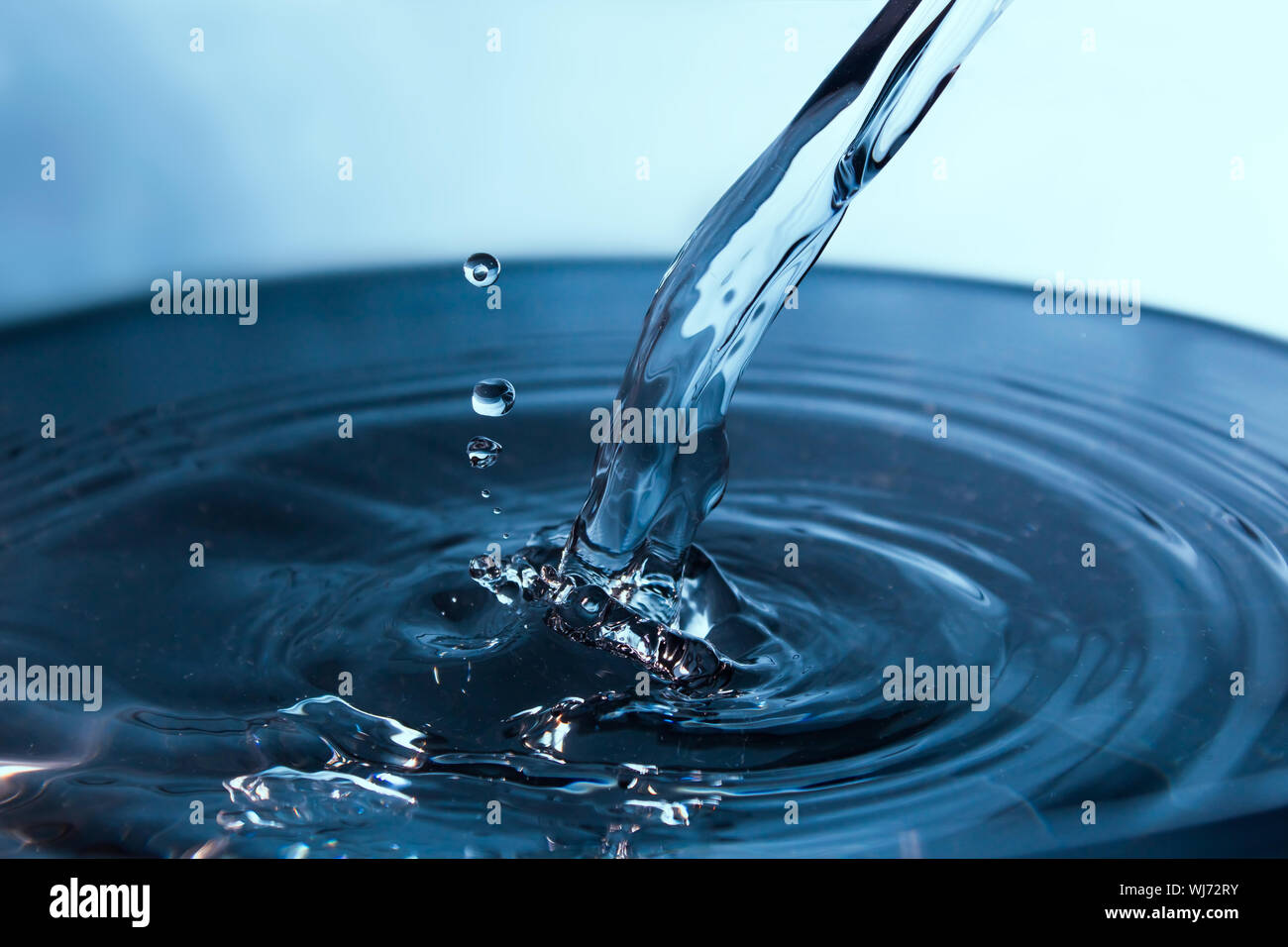 Blue stream of water on a light background. Water pouring into a large ...