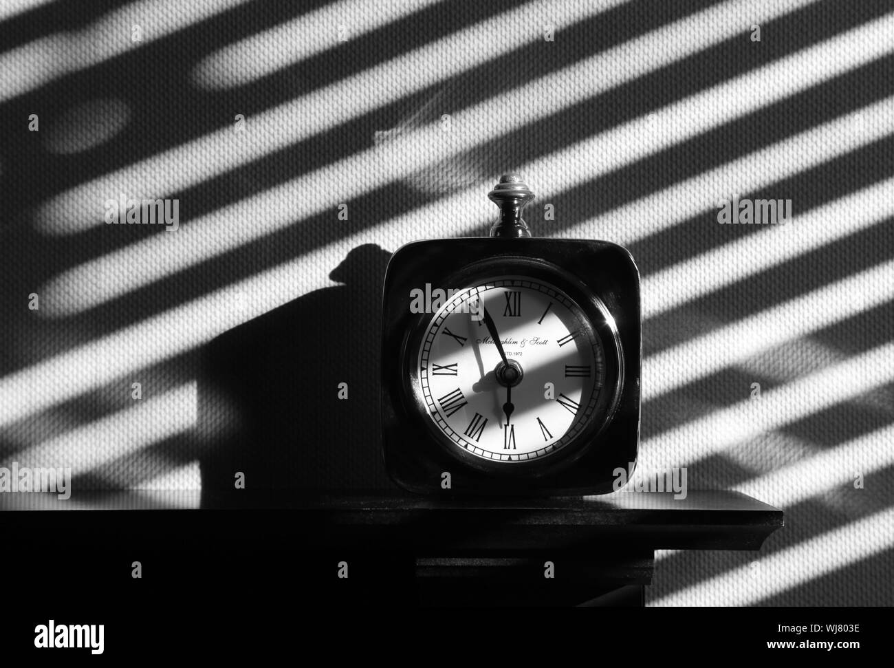 Clock lit by evening light shining through blinds Stock Photo - Alamy