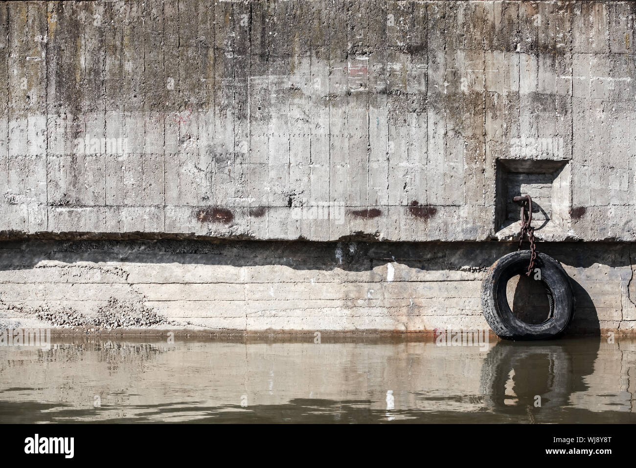 Grungy concrete mooring wall with tire bumper, background photo texture ...